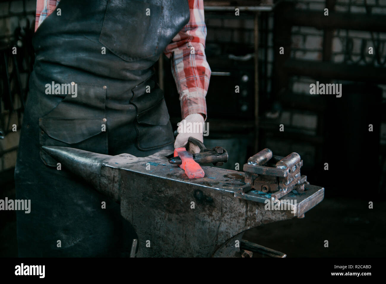 Blacksmith working with red hot metal workpiece of new hammer at anvil ...