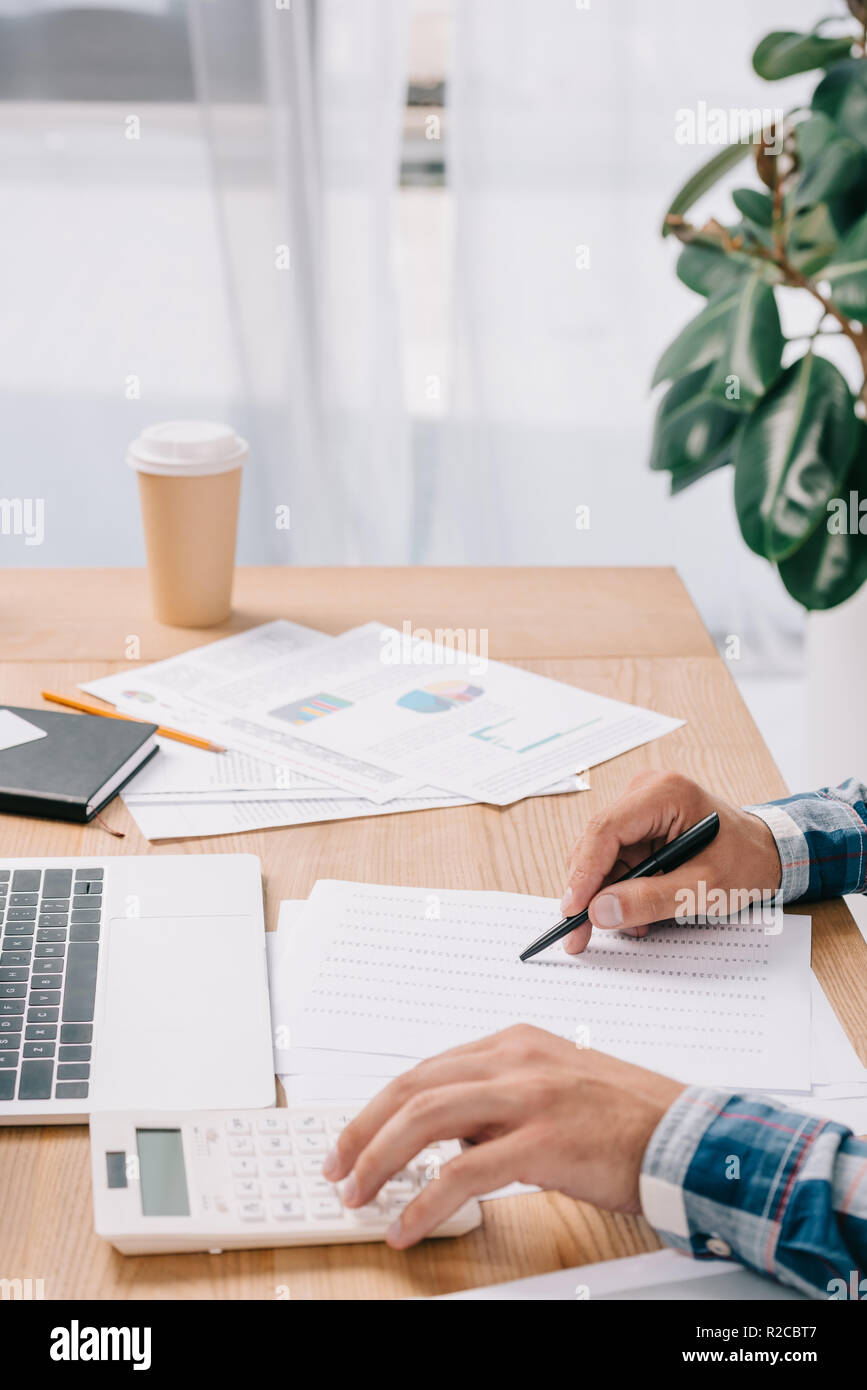 partial view of businessman making calculations at workplace with ...