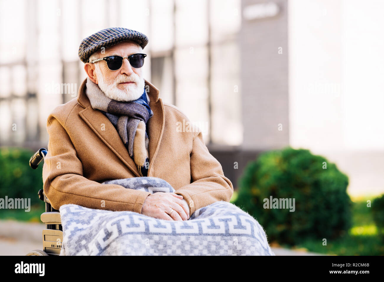 handsome senior disabled man in wheelchair with plaid on legs on street ...