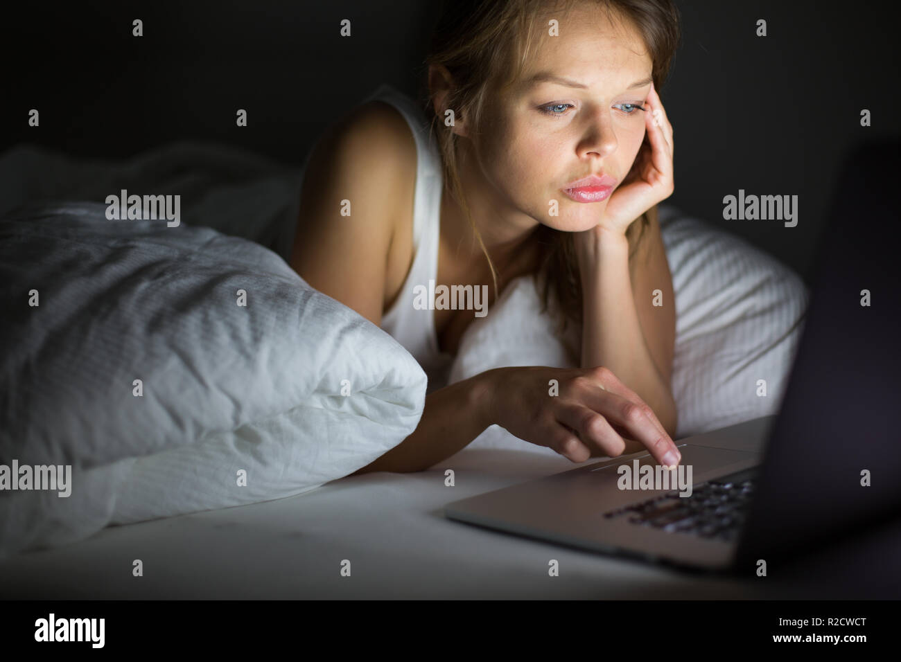 Pretty, young woman using her laptop computer in bed (color toned image ...