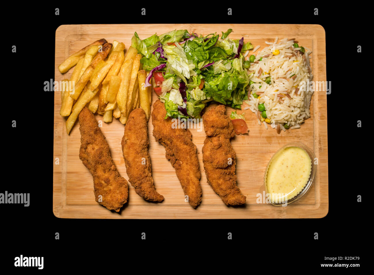 Chicken Goujons served with rice, salad and french friends on wood with ...
