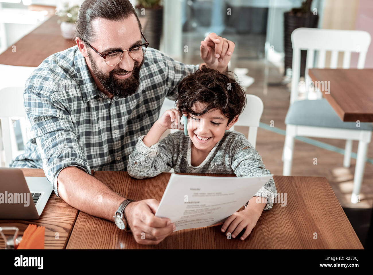 Laughing cute son calling his mother while sitting in restaurant with ...