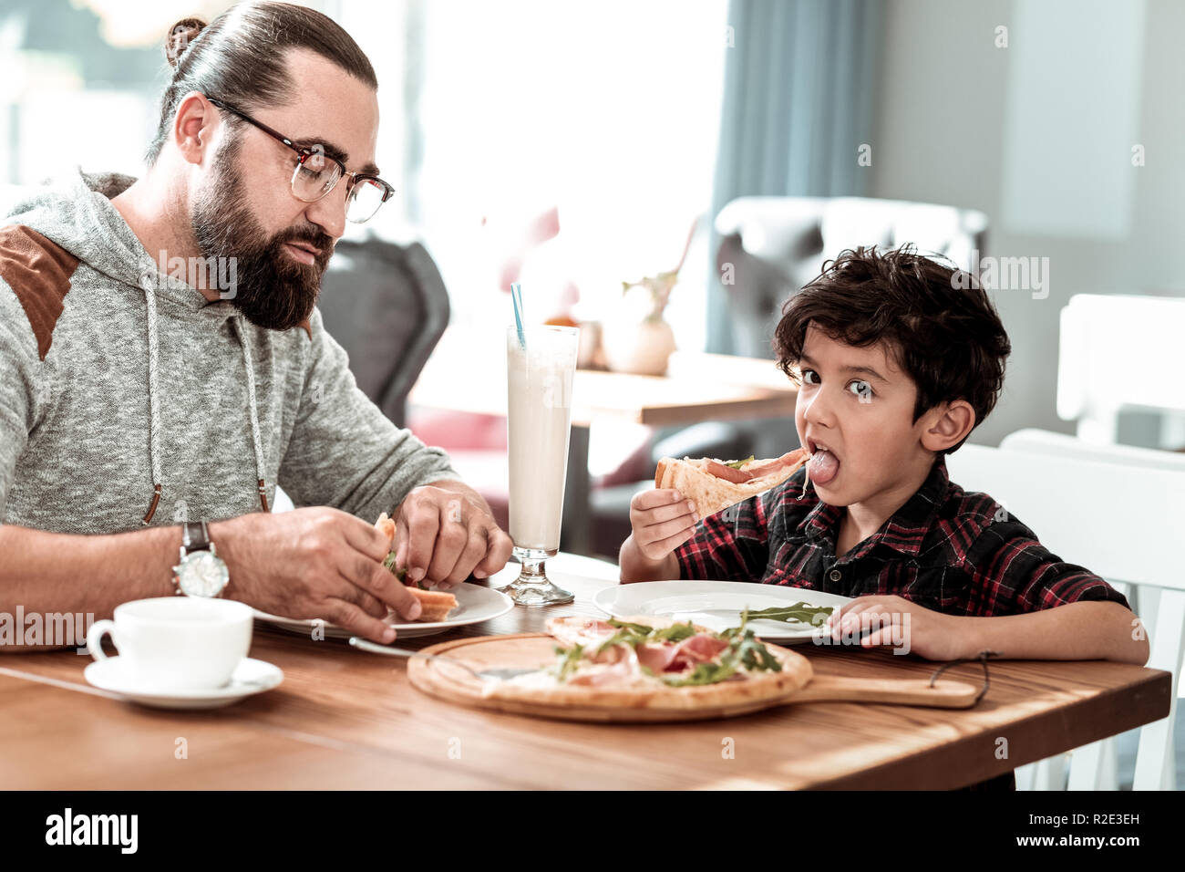 Cute dark-haired son eating yummy cheesy pizza with his father Stock ...
