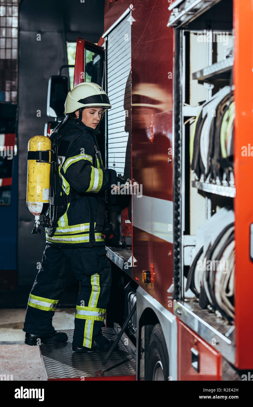 side view of female firefighter with fire extinguisher on back closing ...