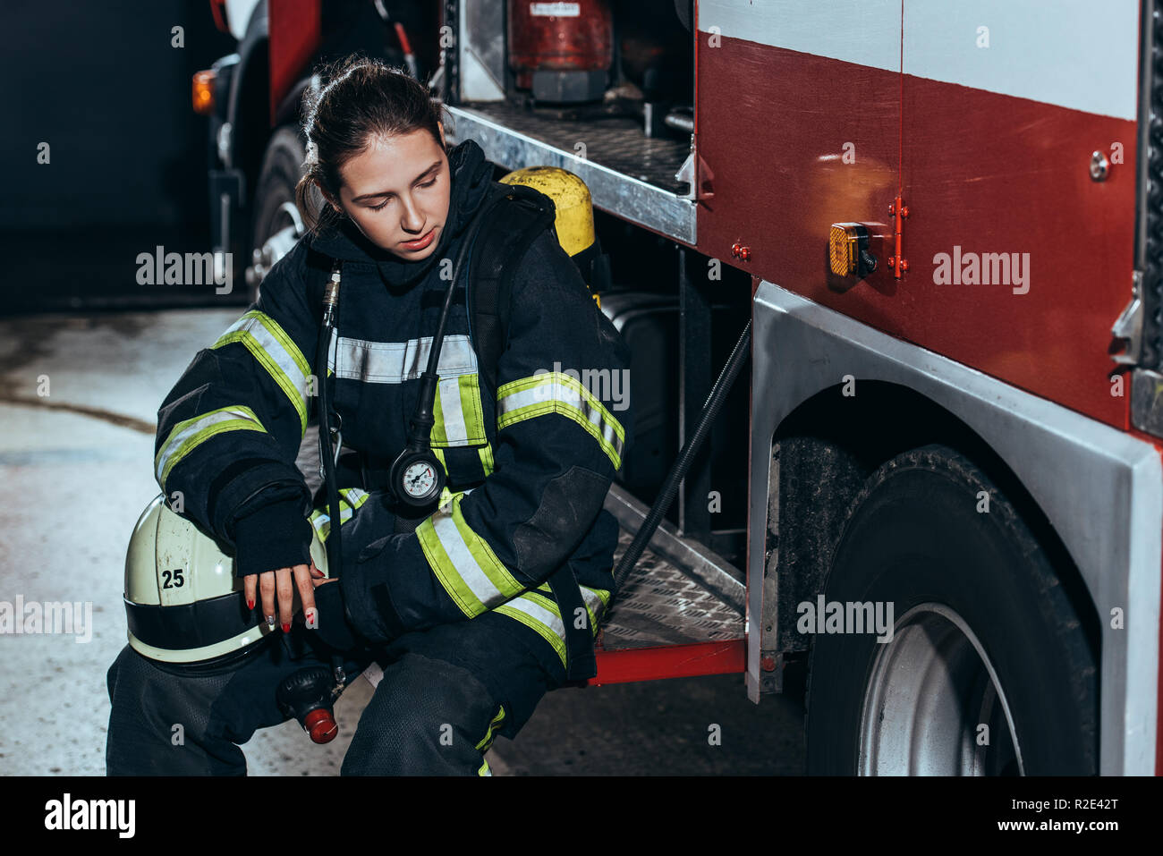 tired female firefighter in uniform with helmet sitting on truck at ...