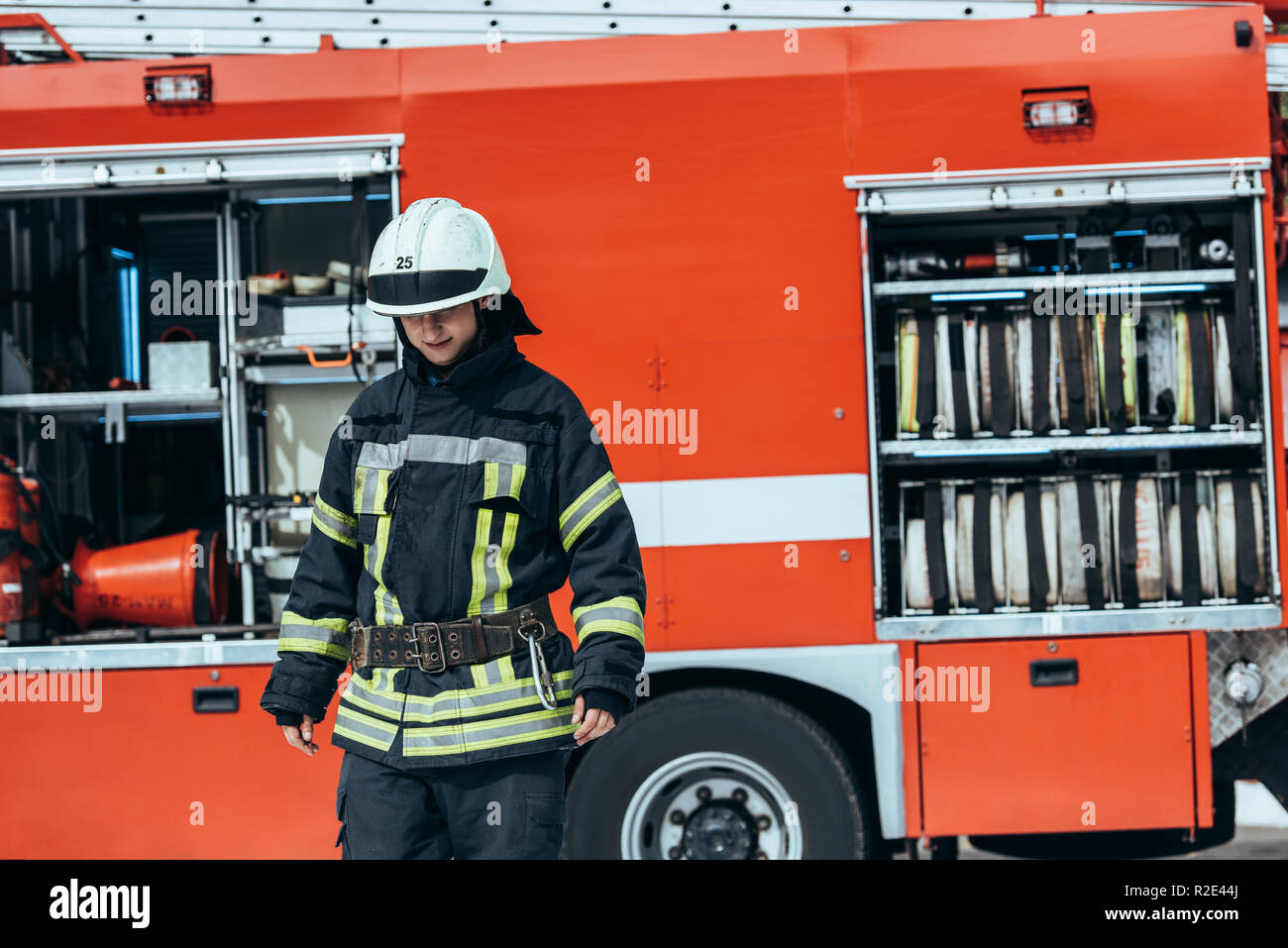 male firefighter in uniform standing on street with red fire truck ...