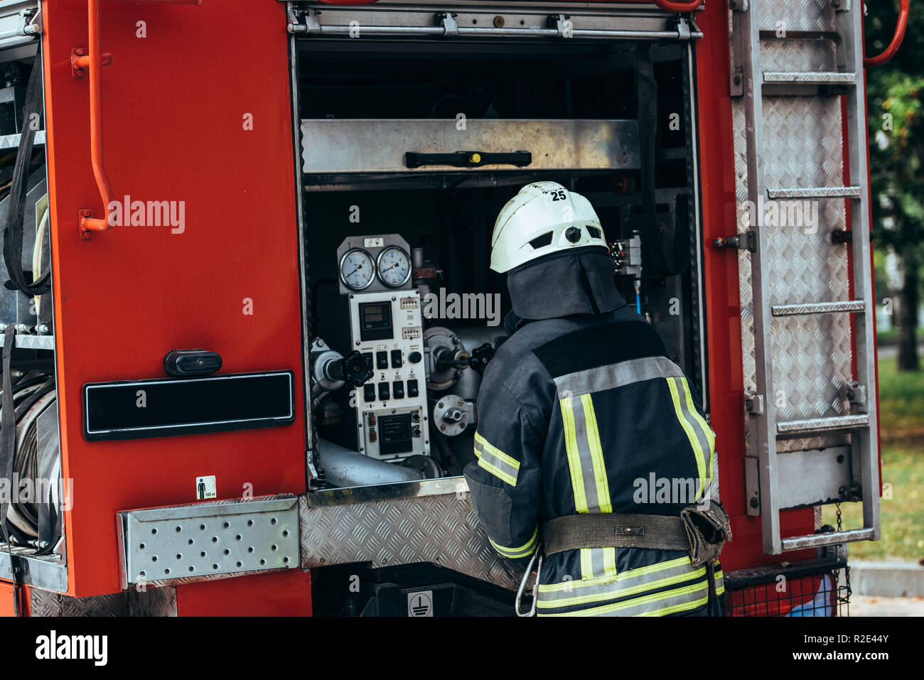 back view of firefighter in uniform and helmet standing at fire truck ...