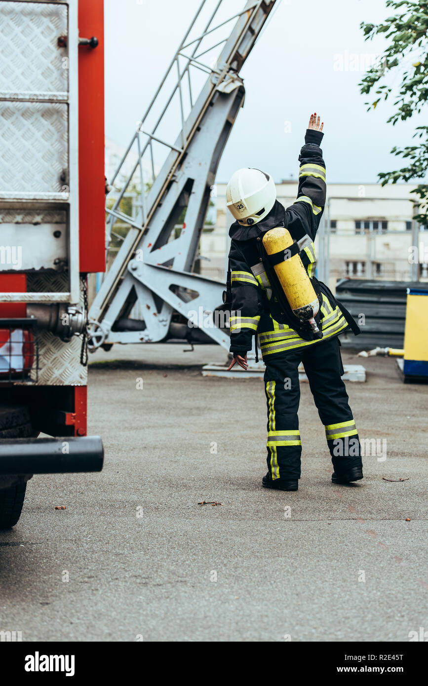 rear view of firefighter in uniform and helmet with fire extinguisher ...
