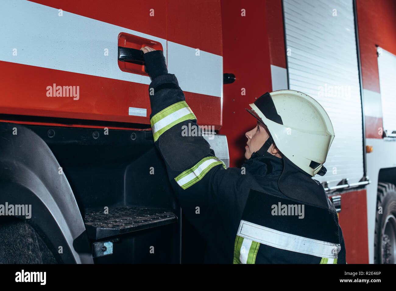 side view of female firefighter holding truck door handle at fire ...