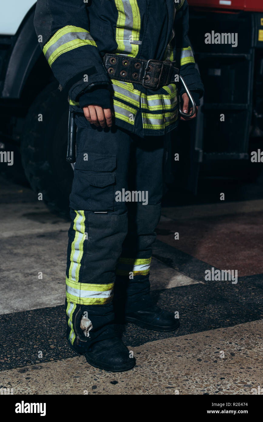 partial view of firefighter in protective fireproof uniform standing at ...