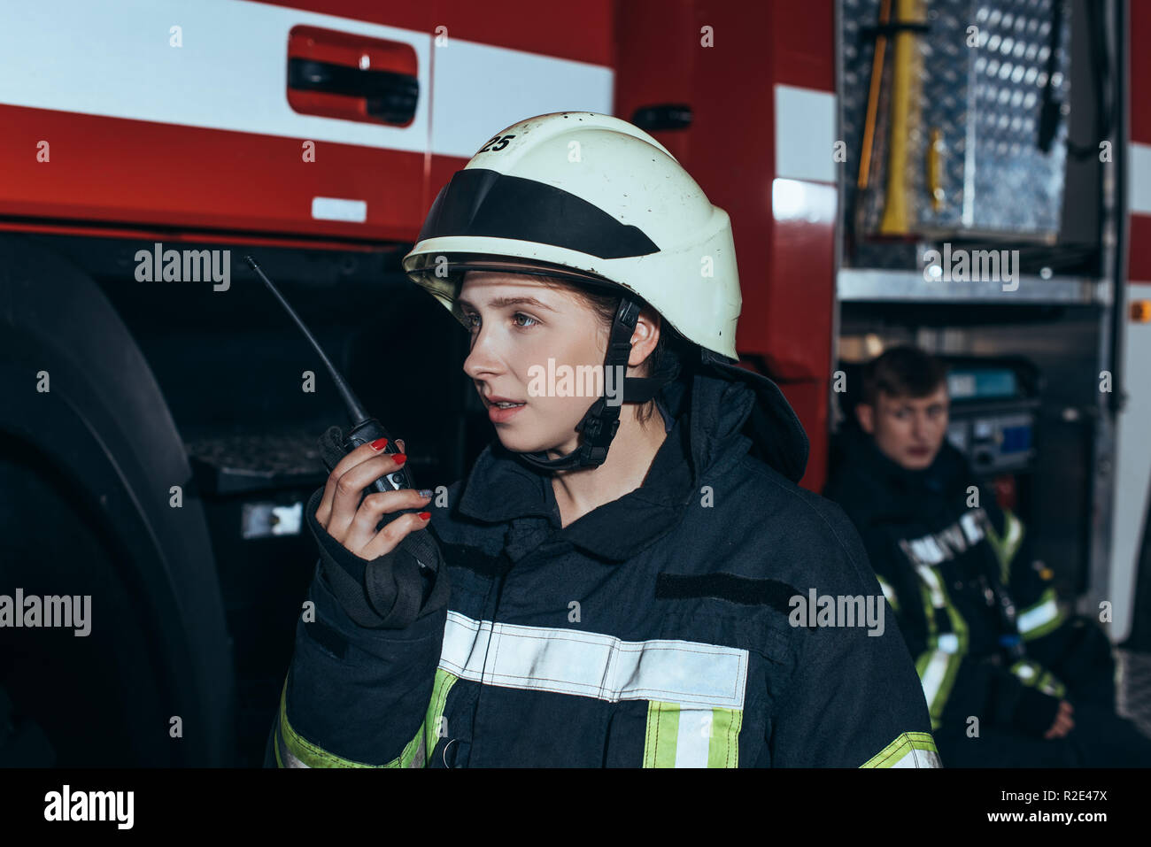 female firefighter talking on portable radio set with colleague behind ...