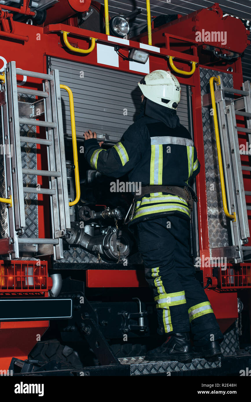 back view of firefighter in fireproof uniform and helmet closing truck ...