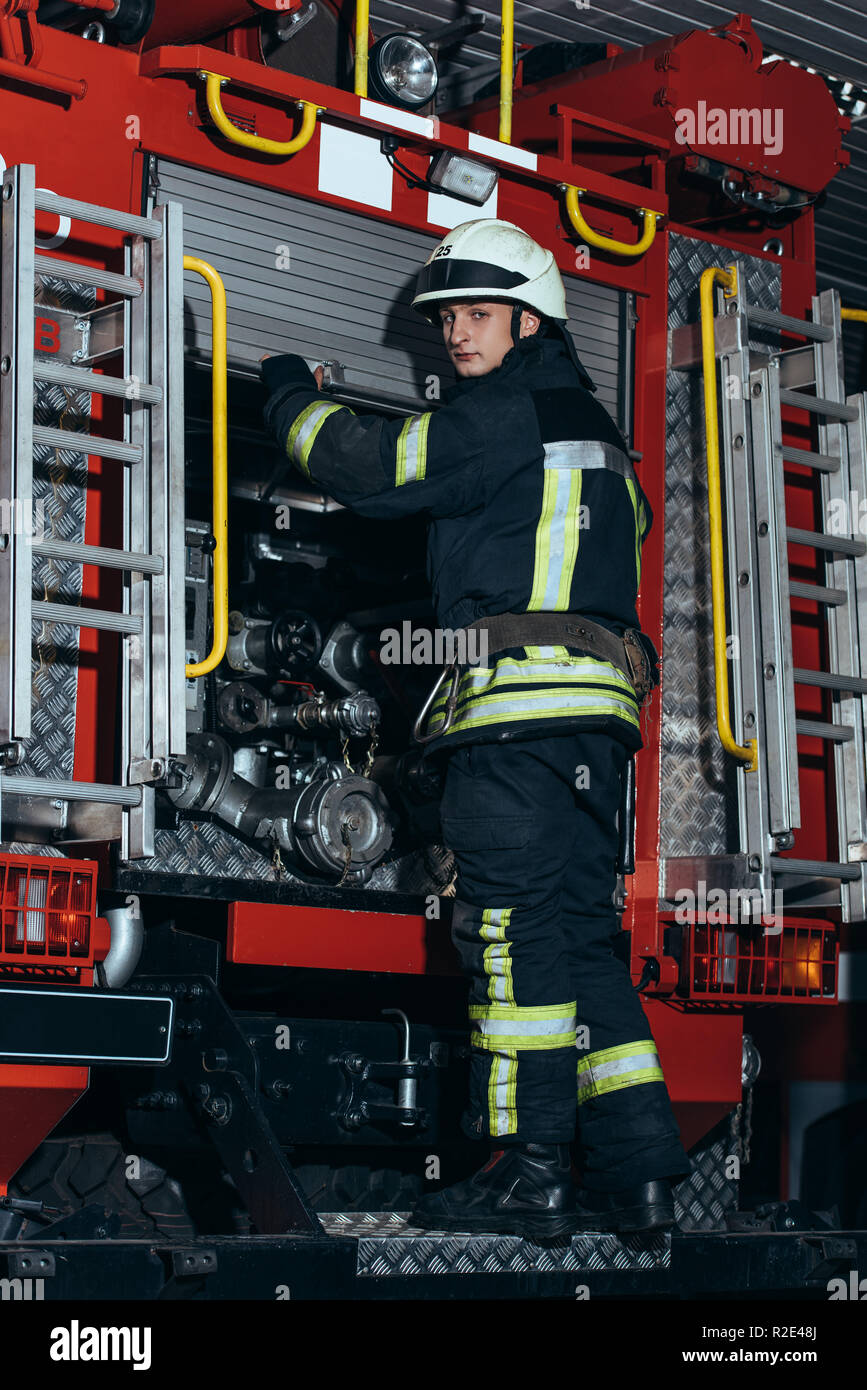fireman in protective uniform and helmet looking at camera at fire ...