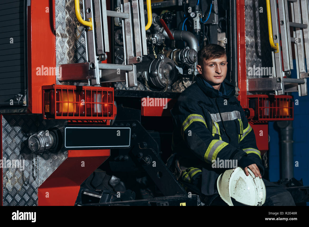 portrait of male firefighter with protective helmet in hands at truck ...