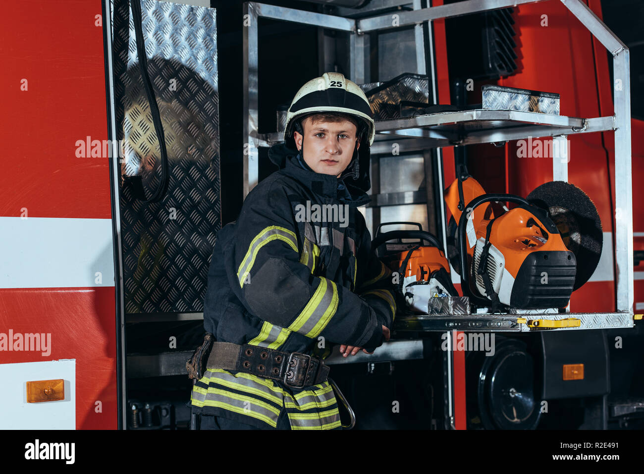 portrait of firefighter in helmet standing at truck at fire station ...
