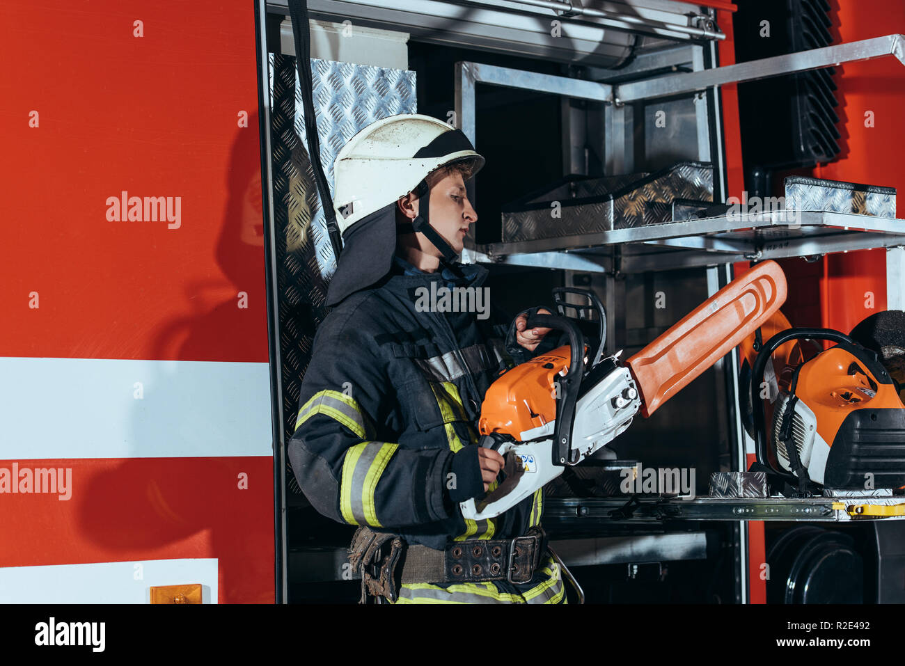 fireman in helmet holding electric saw while standing at truck at fire ...