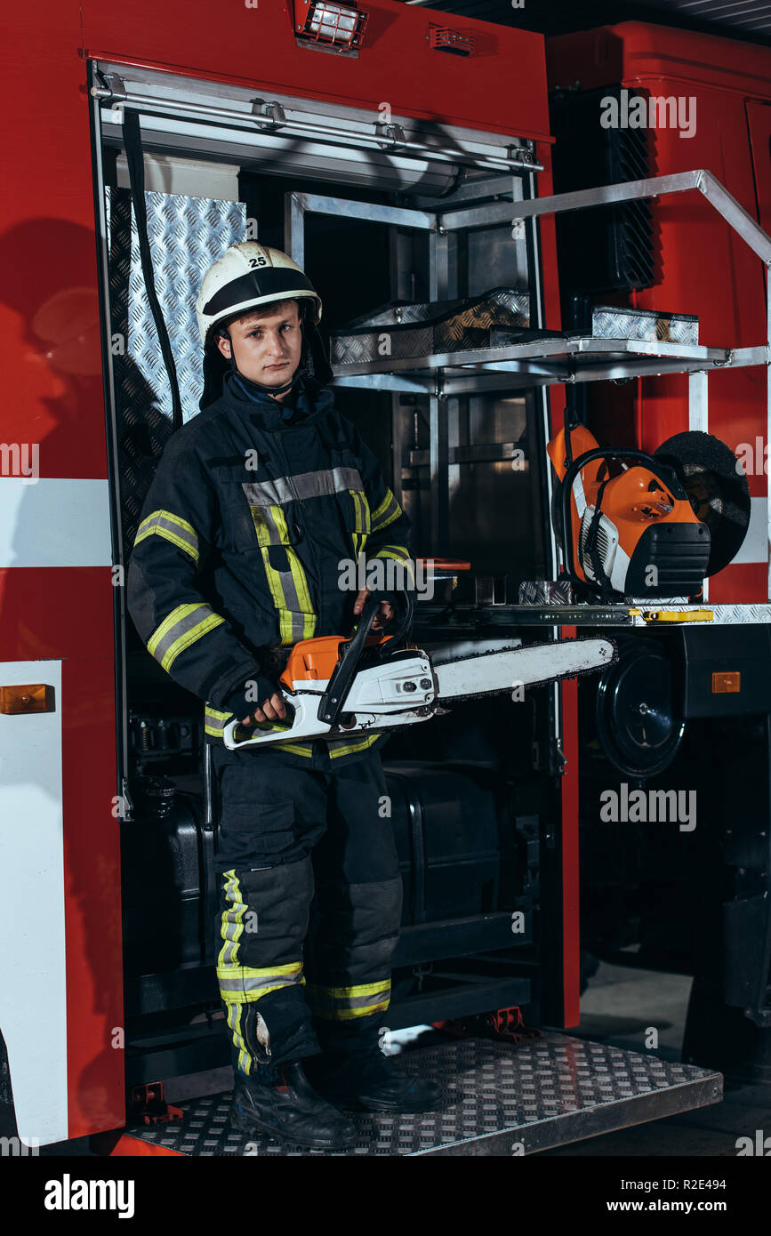 fireman in helmet holding electric saw while standing at truck at fire ...