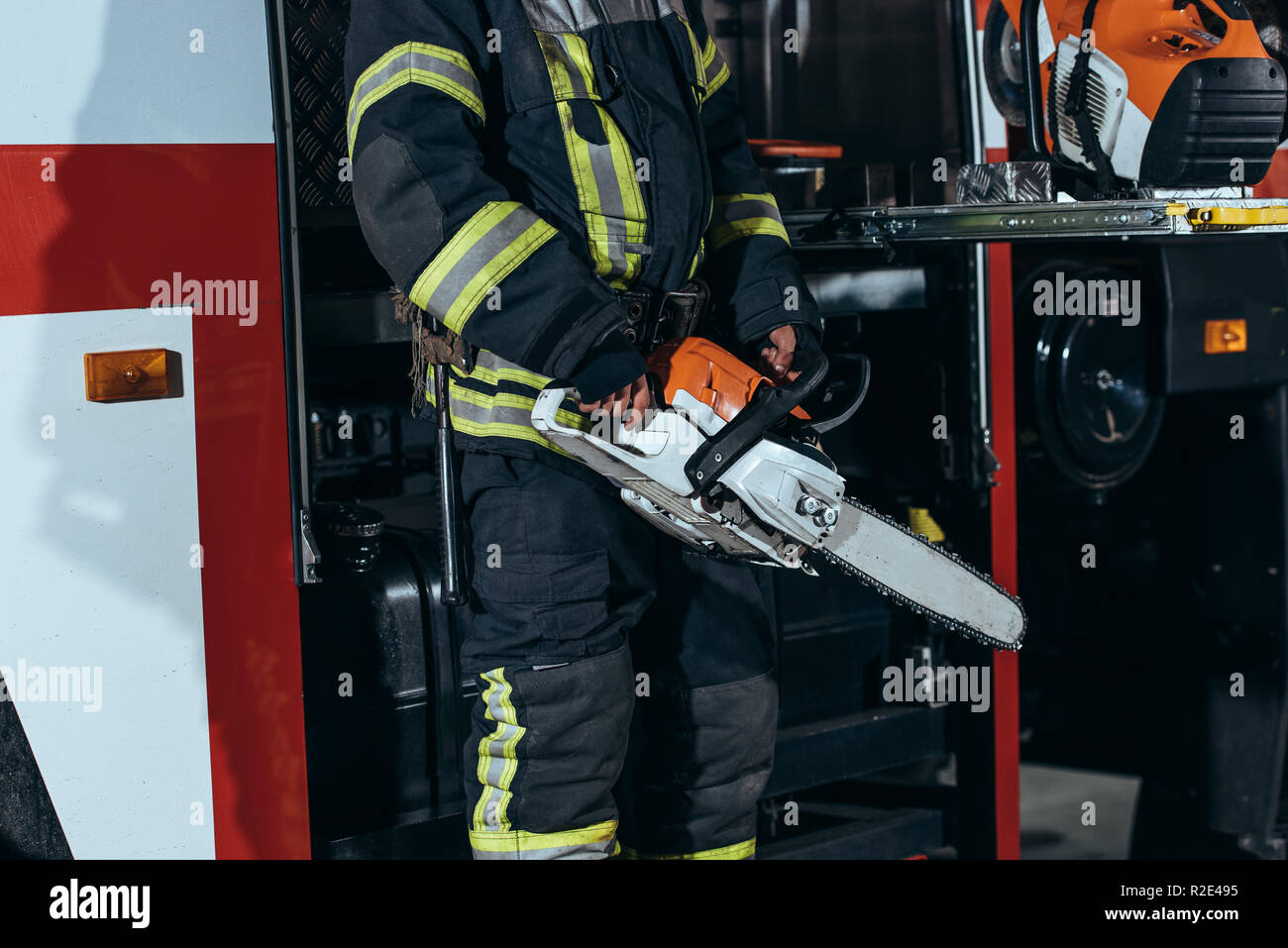 partial view of firefighter in protective uniform holding electric saw ...