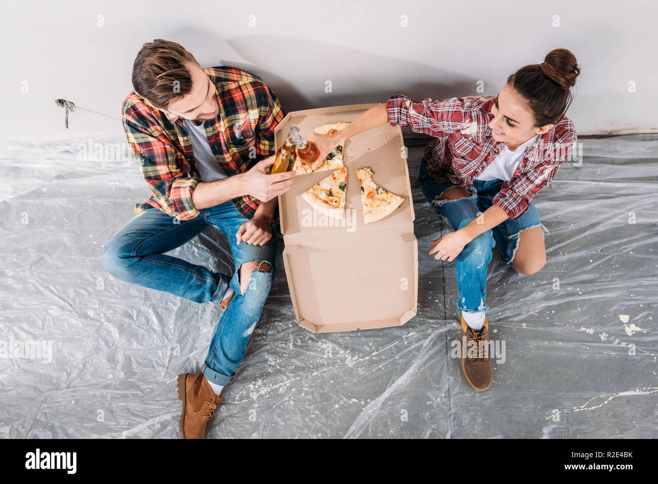 overhead view of young couple clinking beer bottles and eating pizza ...