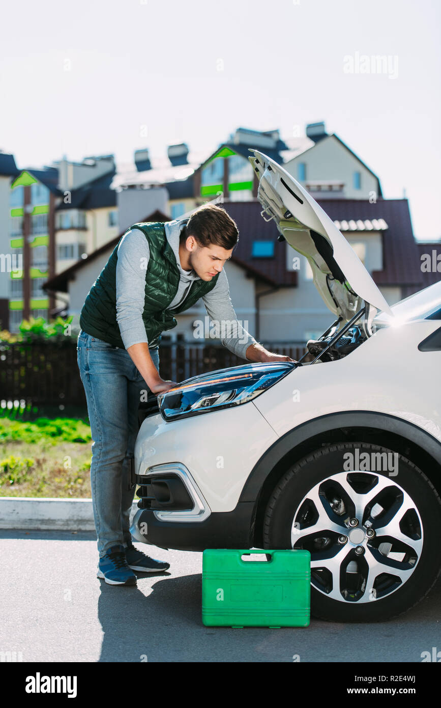 side view of focused young man repairing broken car on street Stock ...