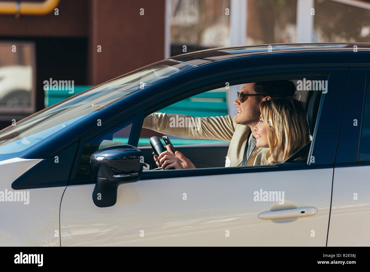 side view of smiling woman driving car with boyfriend near by ...