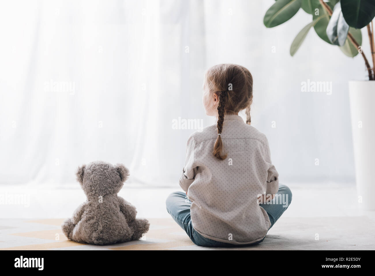 rear view of little child sitting on floor with teddy bear and looking ...