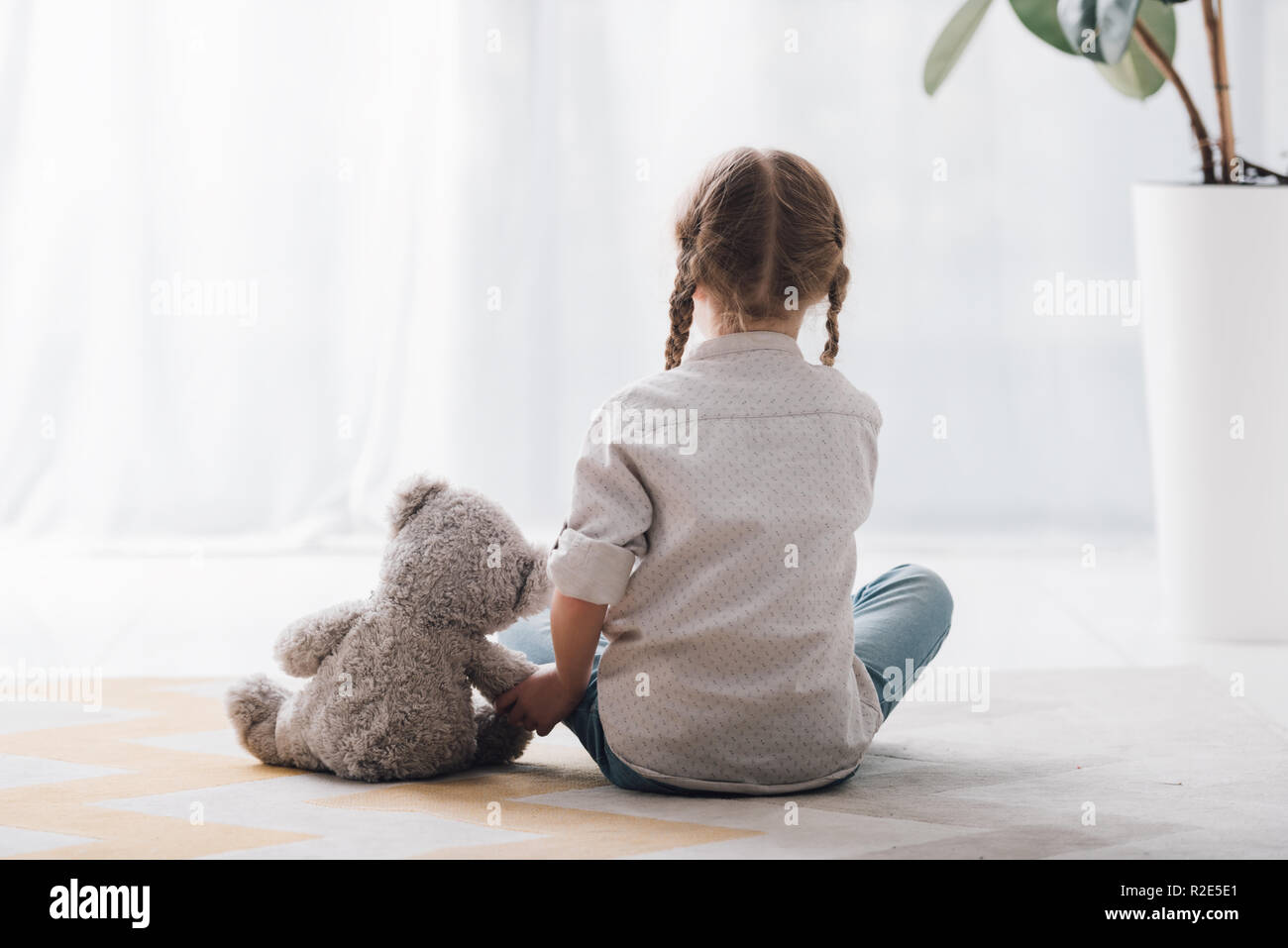 rear view of little child sitting on floor with her teddy bear toy ...