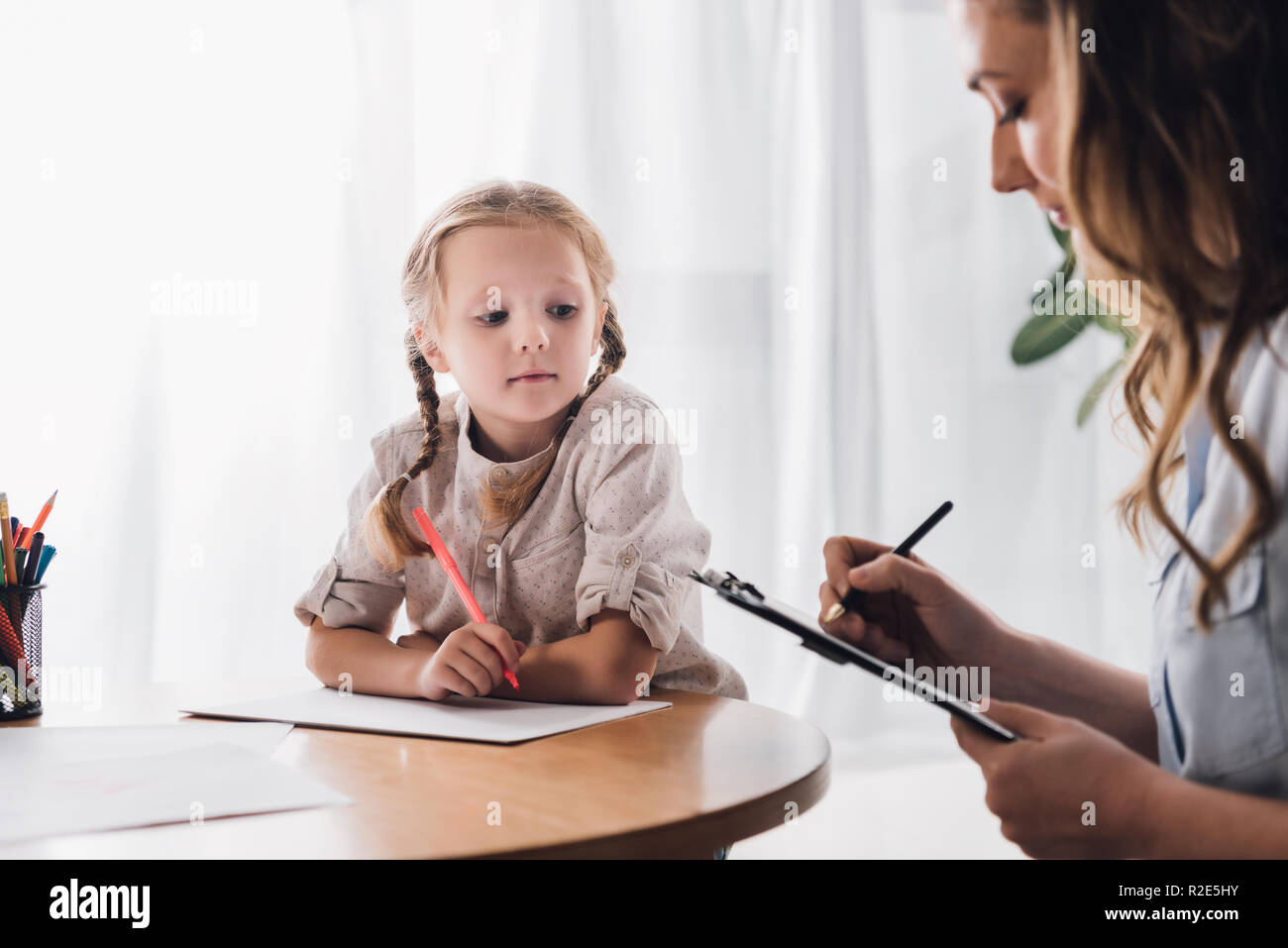 psychologist writing in clipboard while sitting near little drawing ...