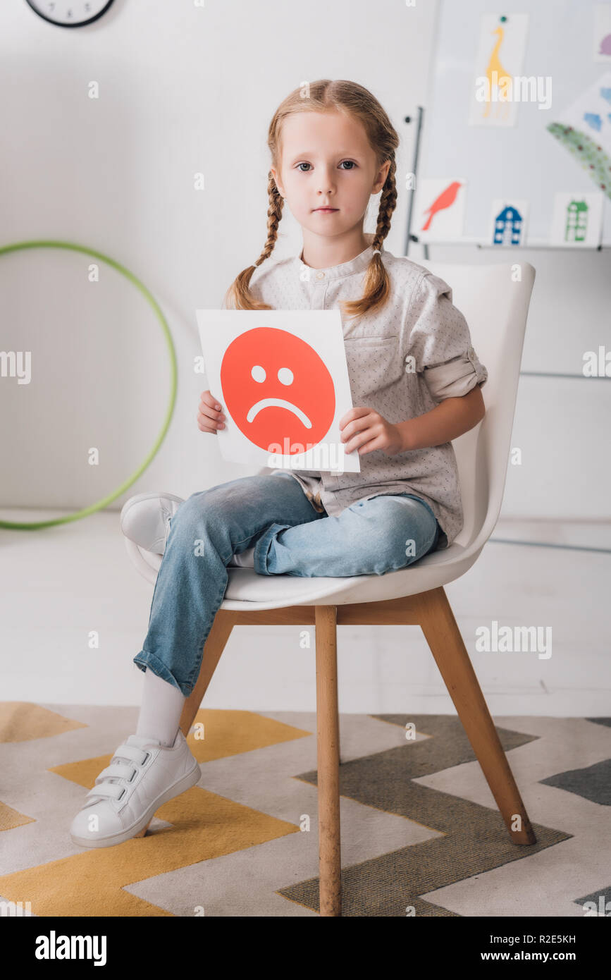 lonely little child sitting on chair holding sad face symbol Stock ...