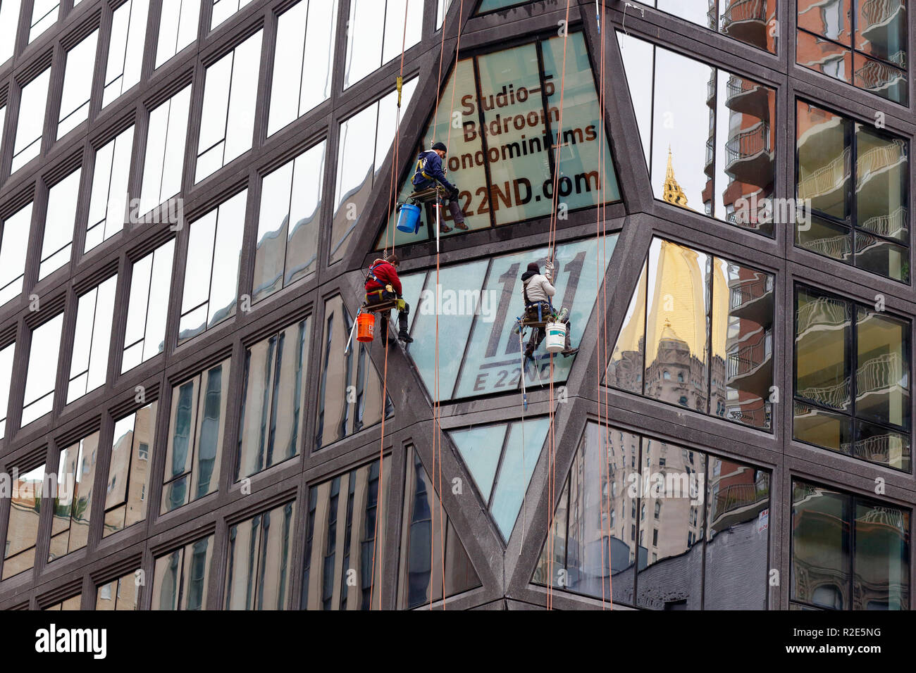 Window washers seated in bosun chairs dangle off a building to clean ...