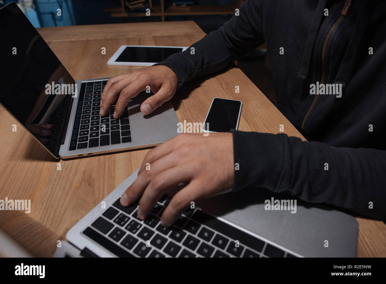 partial view of male hacker using laptops at tabletop with smartphone ...