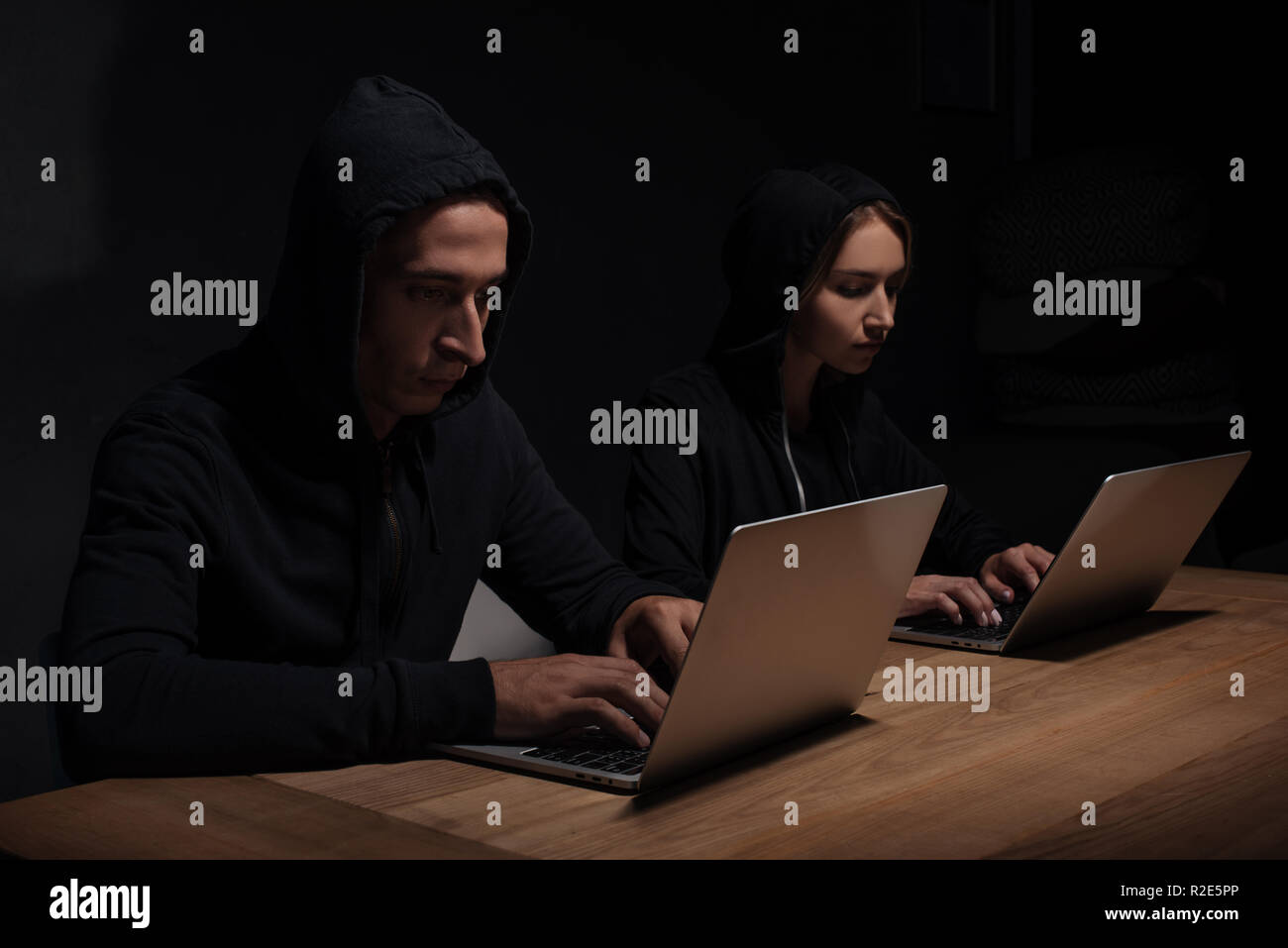 focused hackers in black hoodies using laptops in dark room, cyber ...