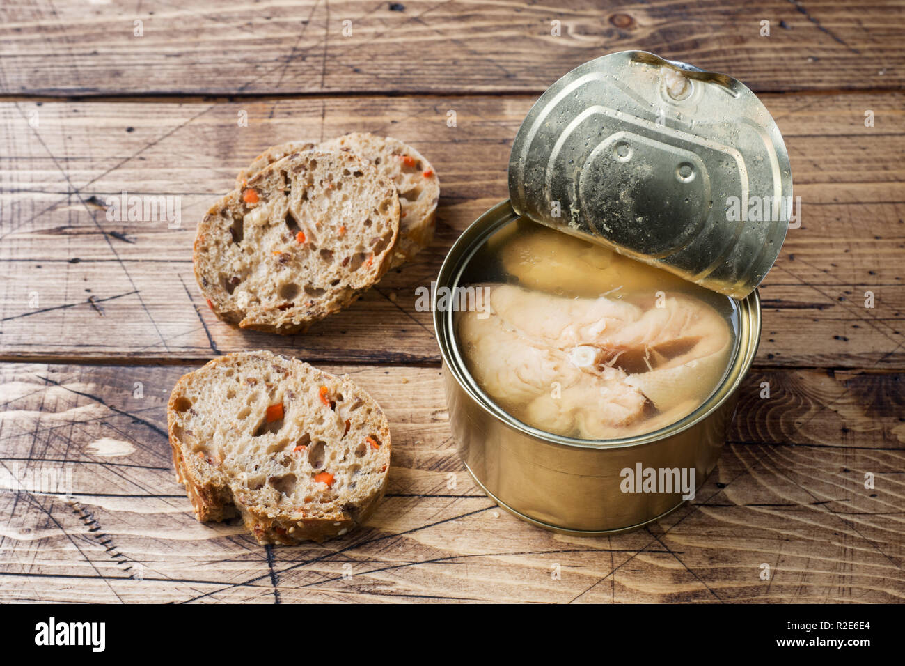 Open tin can with pink salmon fish and pieces of bread on wooden ...