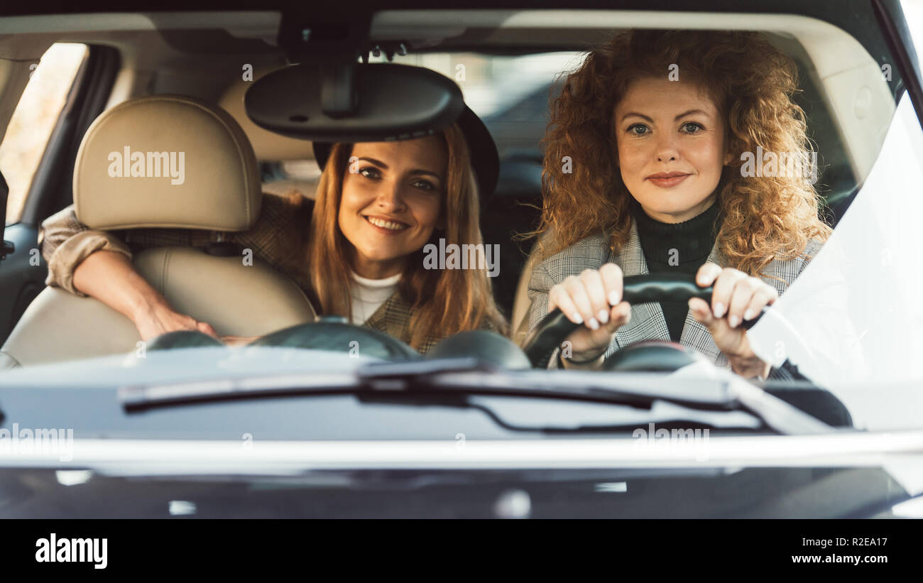 curly ginger woman driving car while her smiling female friend sitting ...