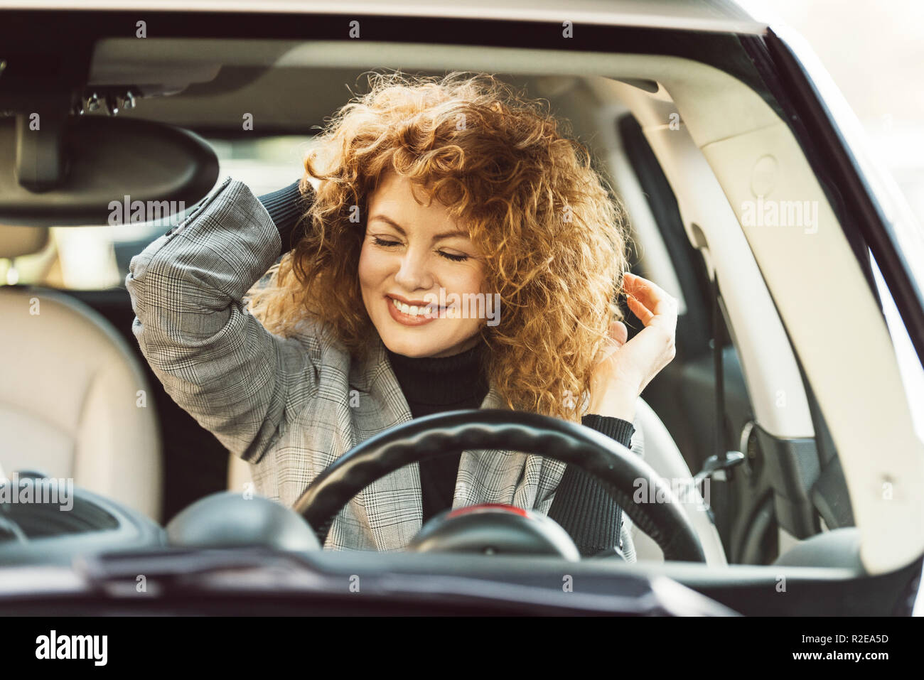 happy beautiful curly ginger woman with closed eyes sitting in car ...