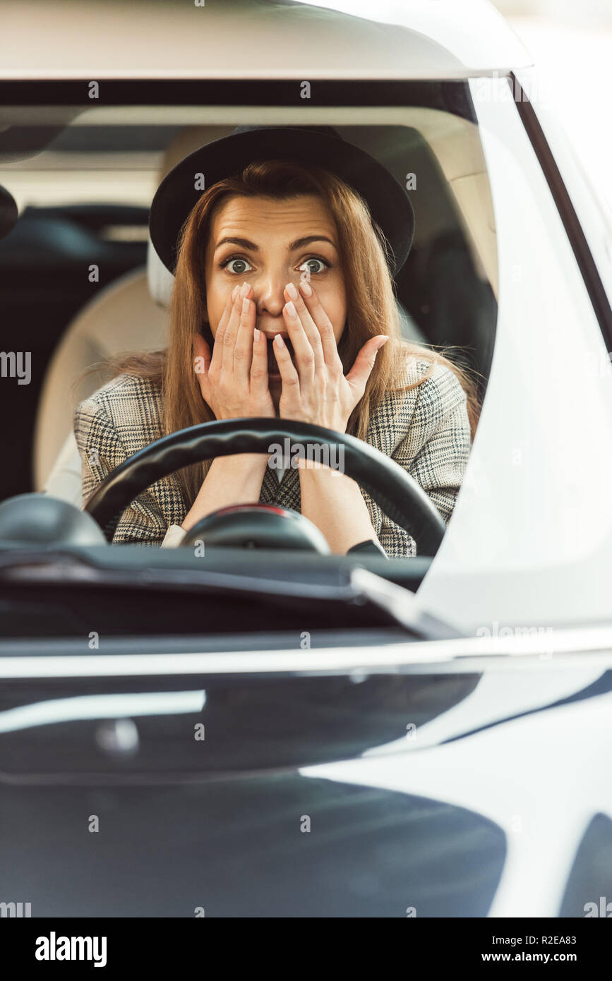 shocked woman gesturing by hands while sitting at steering wheel in car ...