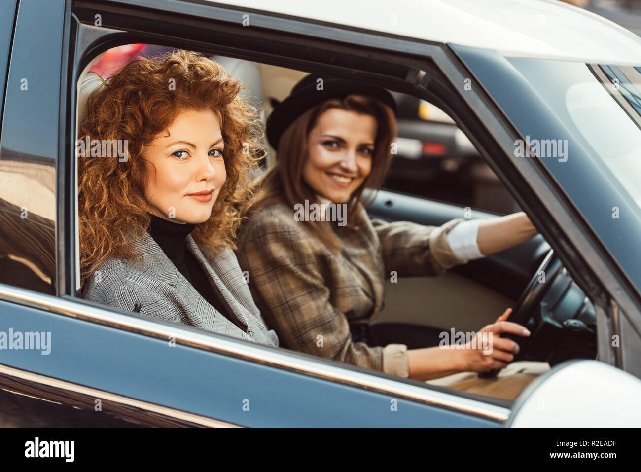 attractive happy woman in black hat driving car while her ginger female ...