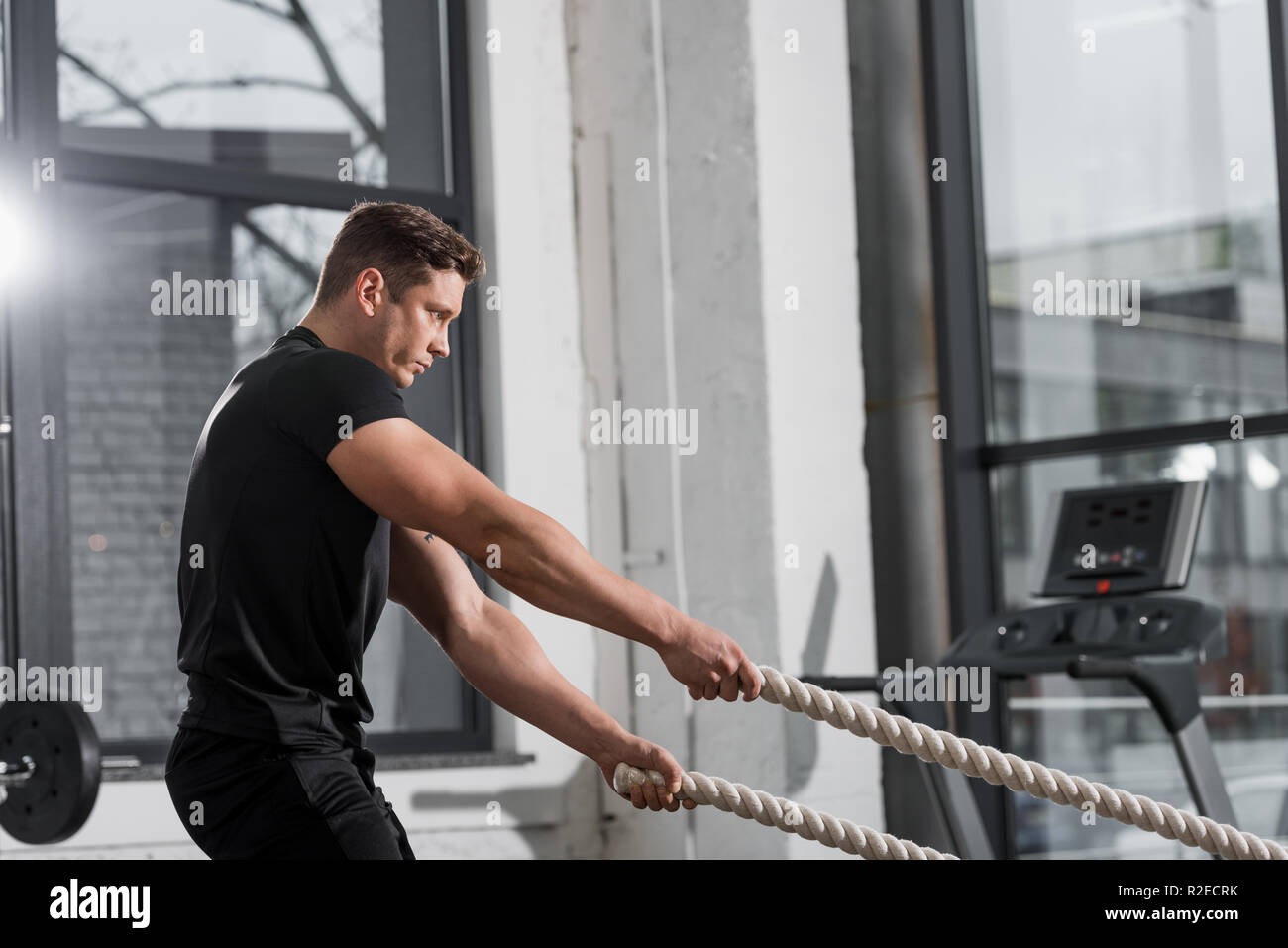 side view of handsome muscular bodybuilder working out with ropes in ...