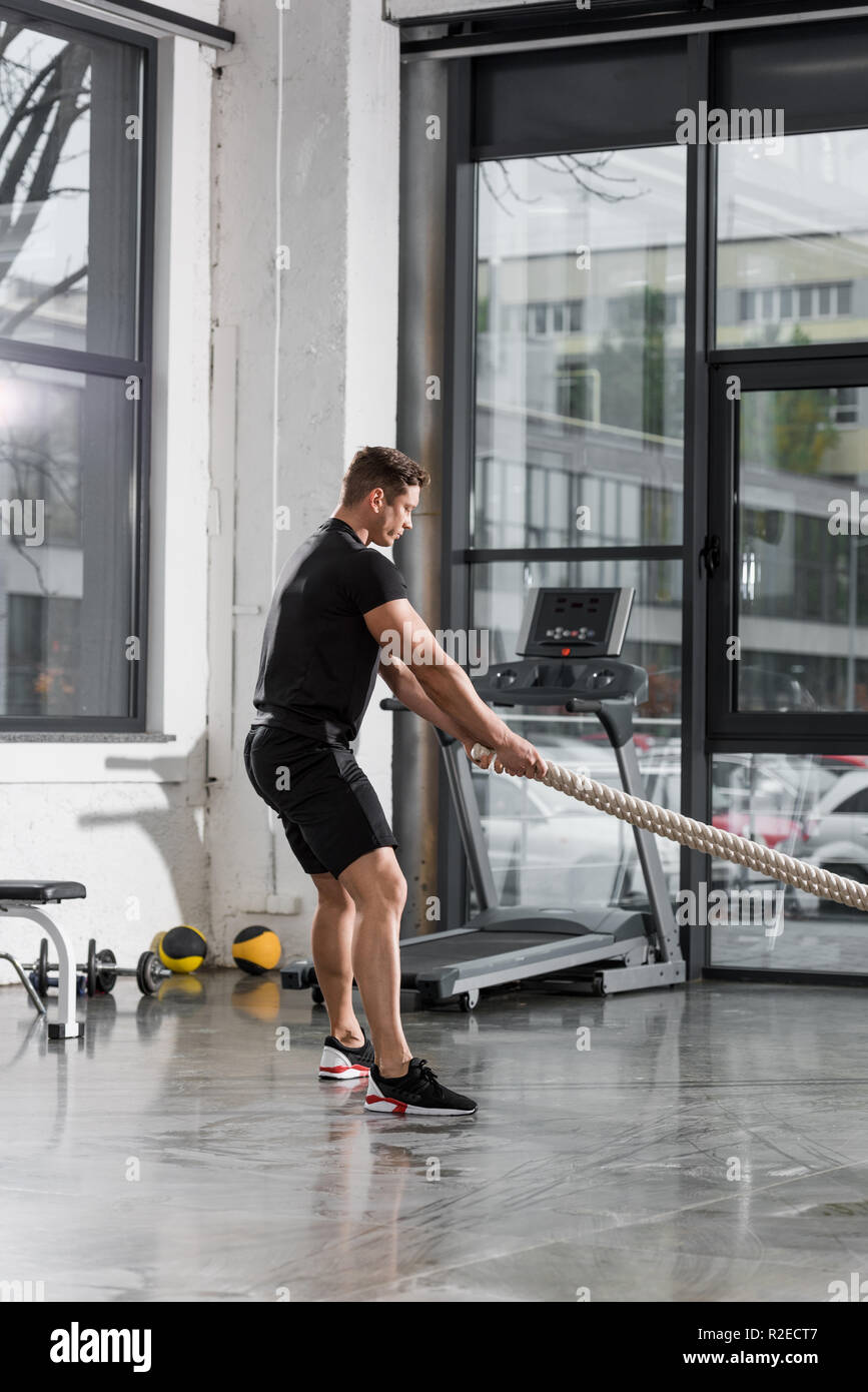 side view of handsome athletic bodybuilder working out with ropes in ...