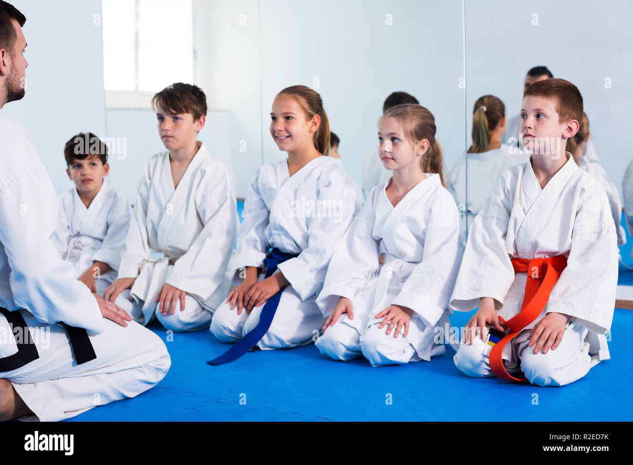 Young smiling man training new karate moves with kids during class ...
