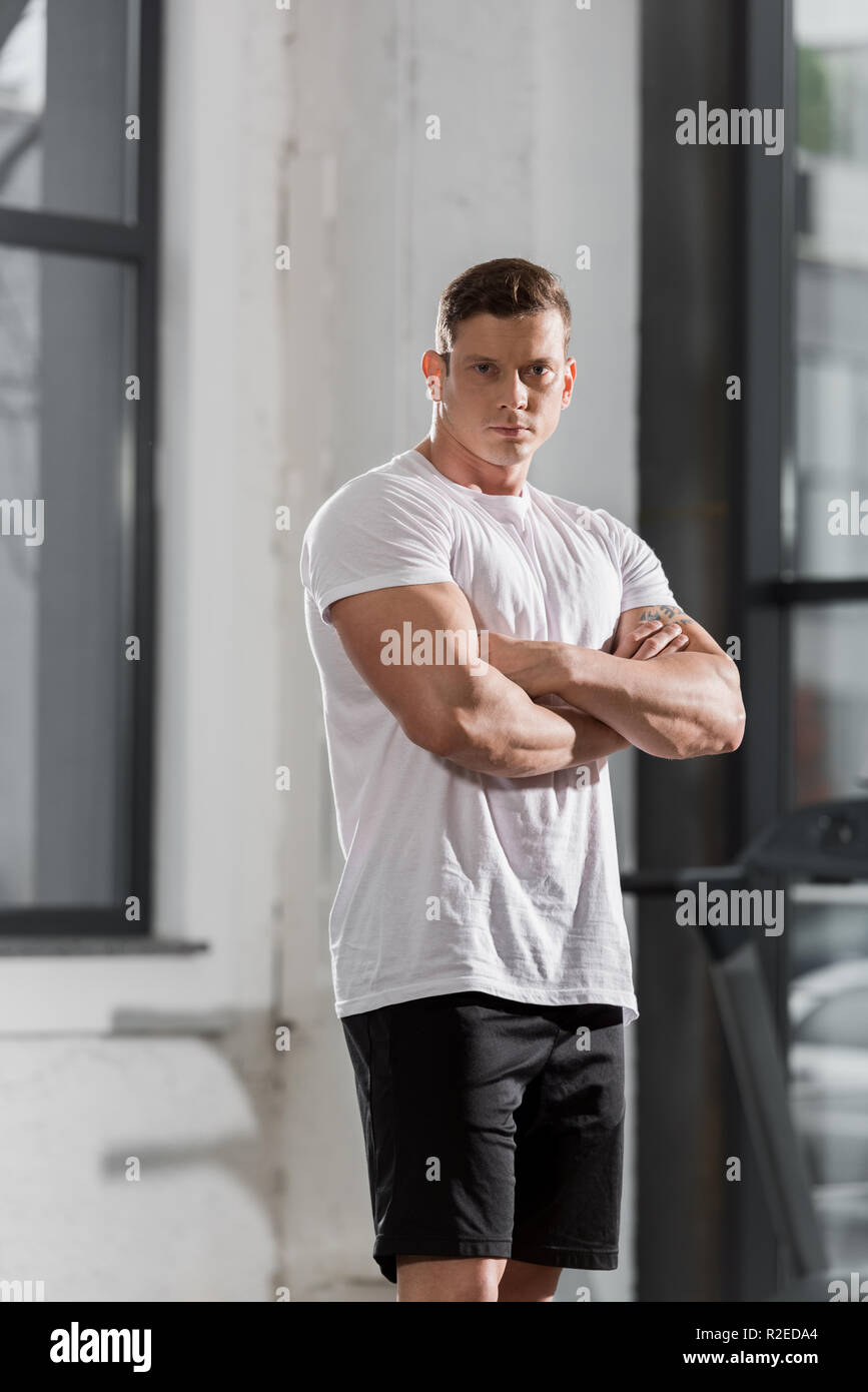 handsome athletic bodybuilder standing with crossed arms and looking at ...