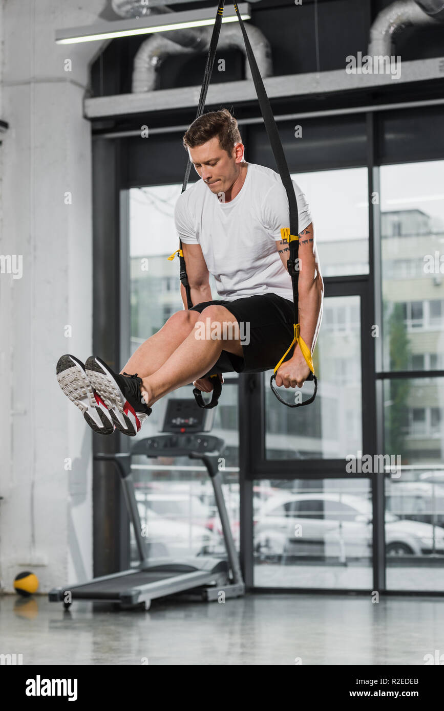 handsome athletic bodybuilder exercising with suspension straps in gym ...