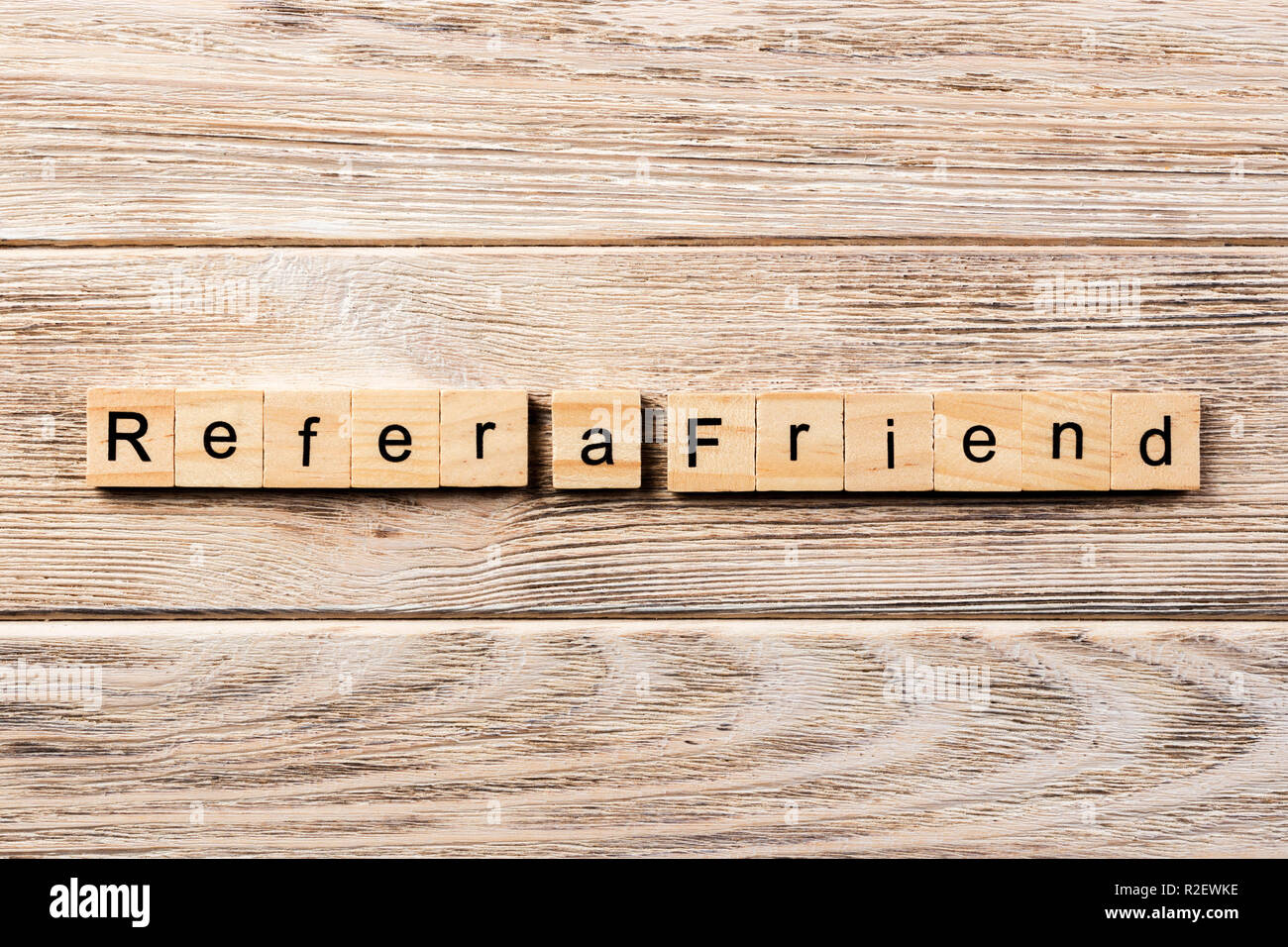 refer a friend word written on wood block. refer a friend text on table ...