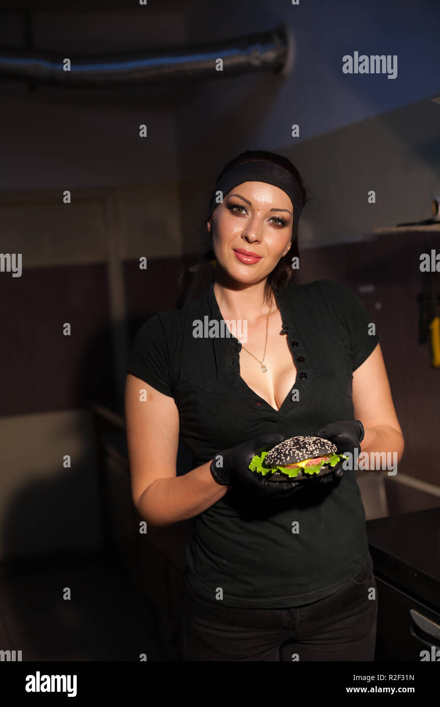 beautiful woman chef prepares a hamburger in the kitchen of the ...