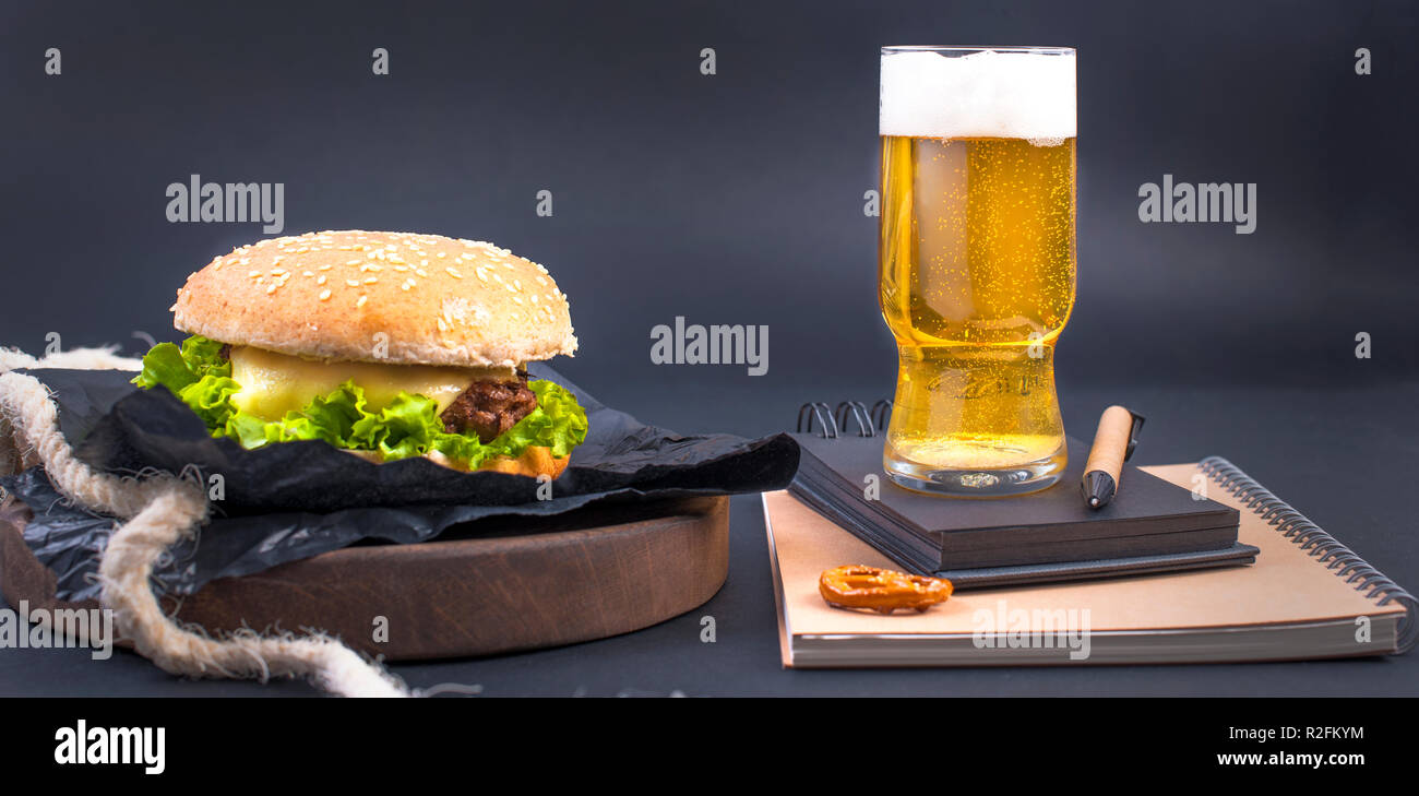 Big hamburger, beer and notebook for planning on a black background ...