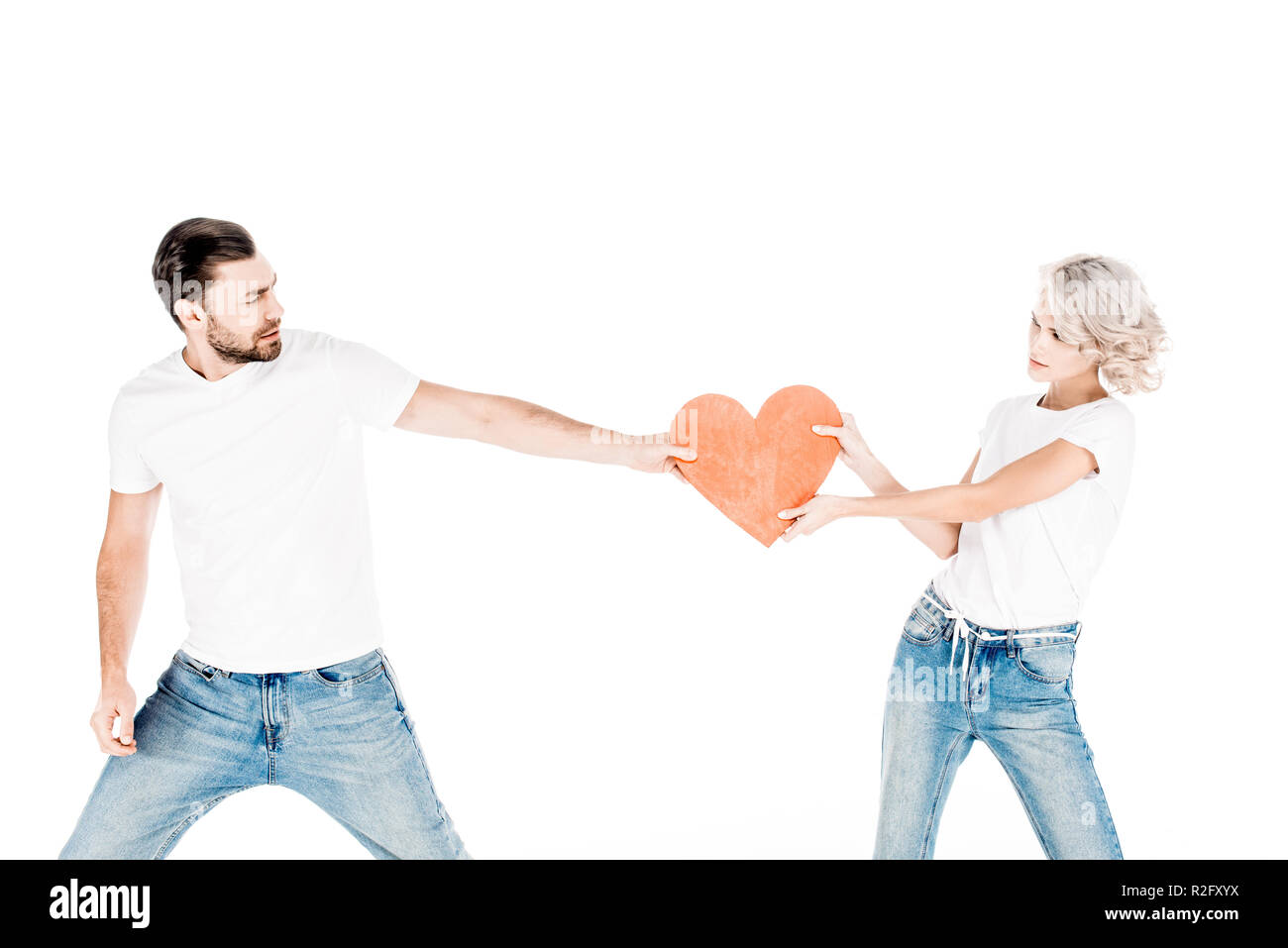 Young adult couple pulling one red big heart shape to each other ...