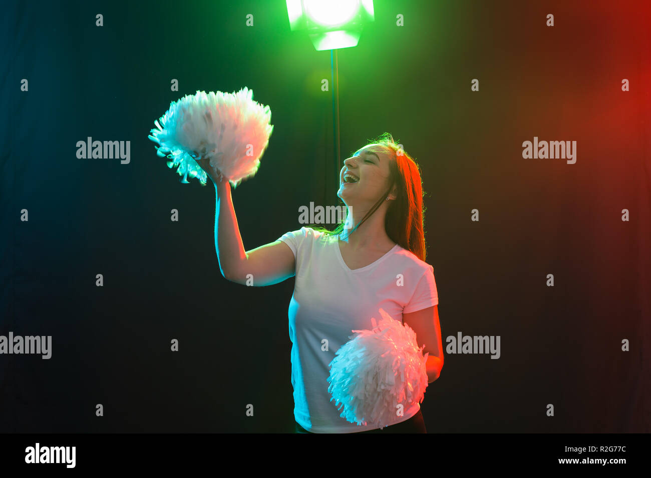 Cheerleading young woman dancing with pom-poms on colourful background ...
