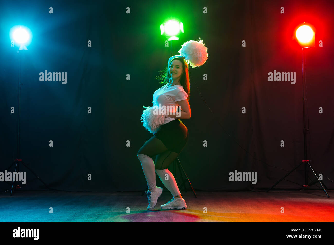 Cheerleading young woman dancing with pom-poms on colourful background ...