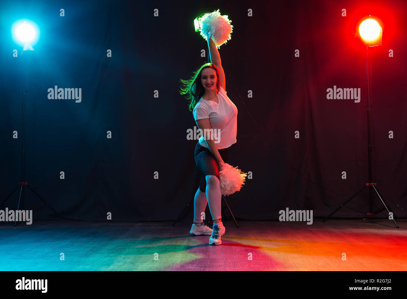 Cheerleading young woman dancing with pom-poms on colourful background ...