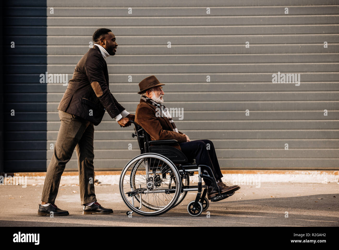Side View Of Senior Disabled Man In Wheelchair And African American Man